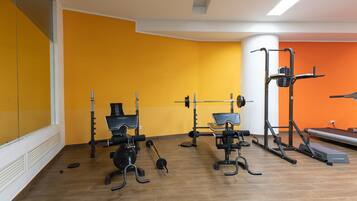 Uma academia com diversos equipamentos de exercício, incluindo uma barra de supino, um suporte para agachamento e uma esteira.