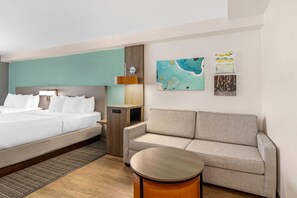 Quarto de hotel com cama, sofá, mesinha e obras de arte na parede.