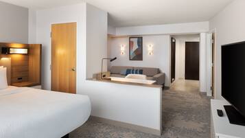 Quarto de hotel com cama, escrivaninha, sofá e televisão.