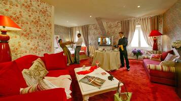 Quarto de hotel com um sofá vermelho, uma mesa de jantar e uma televisão.