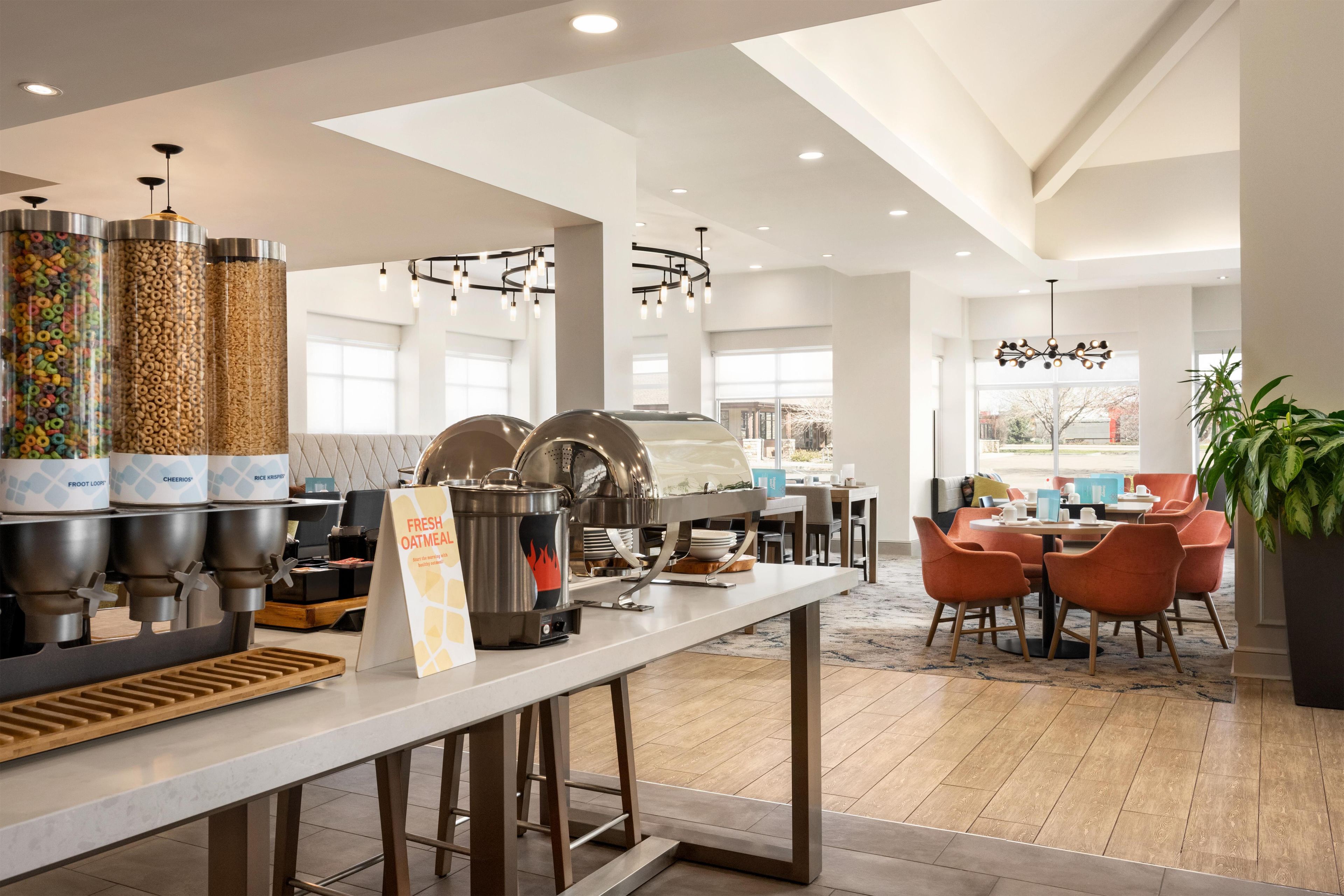 Uma área de café da manhã moderna com buffet, mesas e vista para o exterior.
