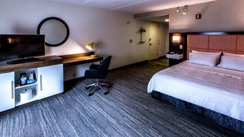 Quarto de hotel com cama, escrivaninha, cadeira, televisão e minibar.