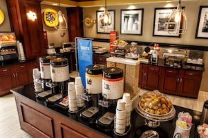 Uma área de buffet com diversos pontos de comida, incluindo uma máquina de café, opção de café descafeinado e uma variedade de doces e produtos de panificação.
