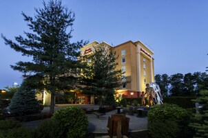 Um hotel com uma placa chamativa, vários andares e área externa bem cuidada, com árvores e uma estátua.