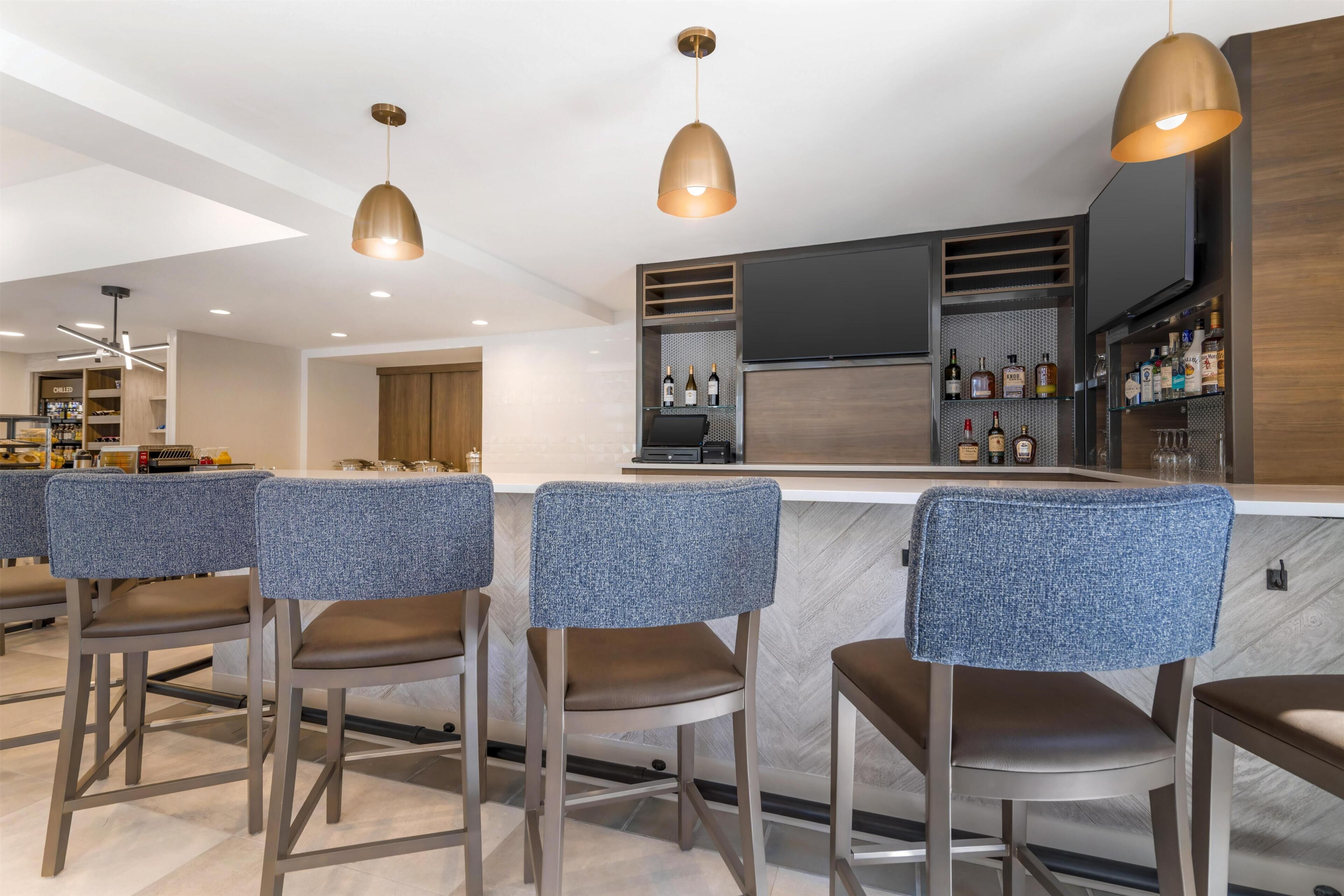 Uma área de bar moderna com banquetas, iluminação pendente e adega.