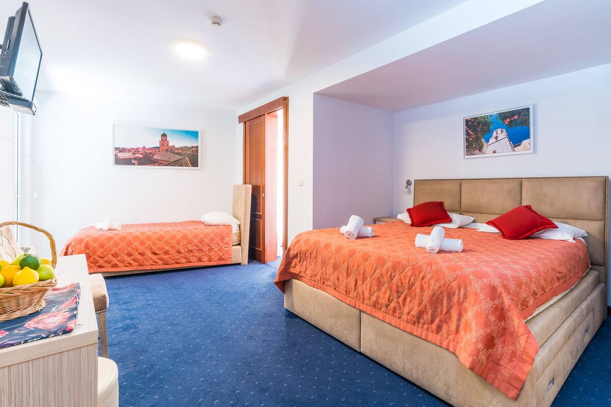 Quarto de hotel com duas camas, uma escrivaninha com uma cesta de frutas e obras de arte nas paredes.