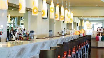 Uma área de bar com um balcão longo, várias luminárias pendentes e fileiras de banquetas.