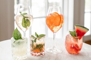 Quatro coquetéis diferentes em copos variados, cada um decorado com uma folha de hortelã e uma fatia de fruta.