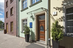 Entrada de um hotel com fachada verde, porta de madeira e placa com o número 3.