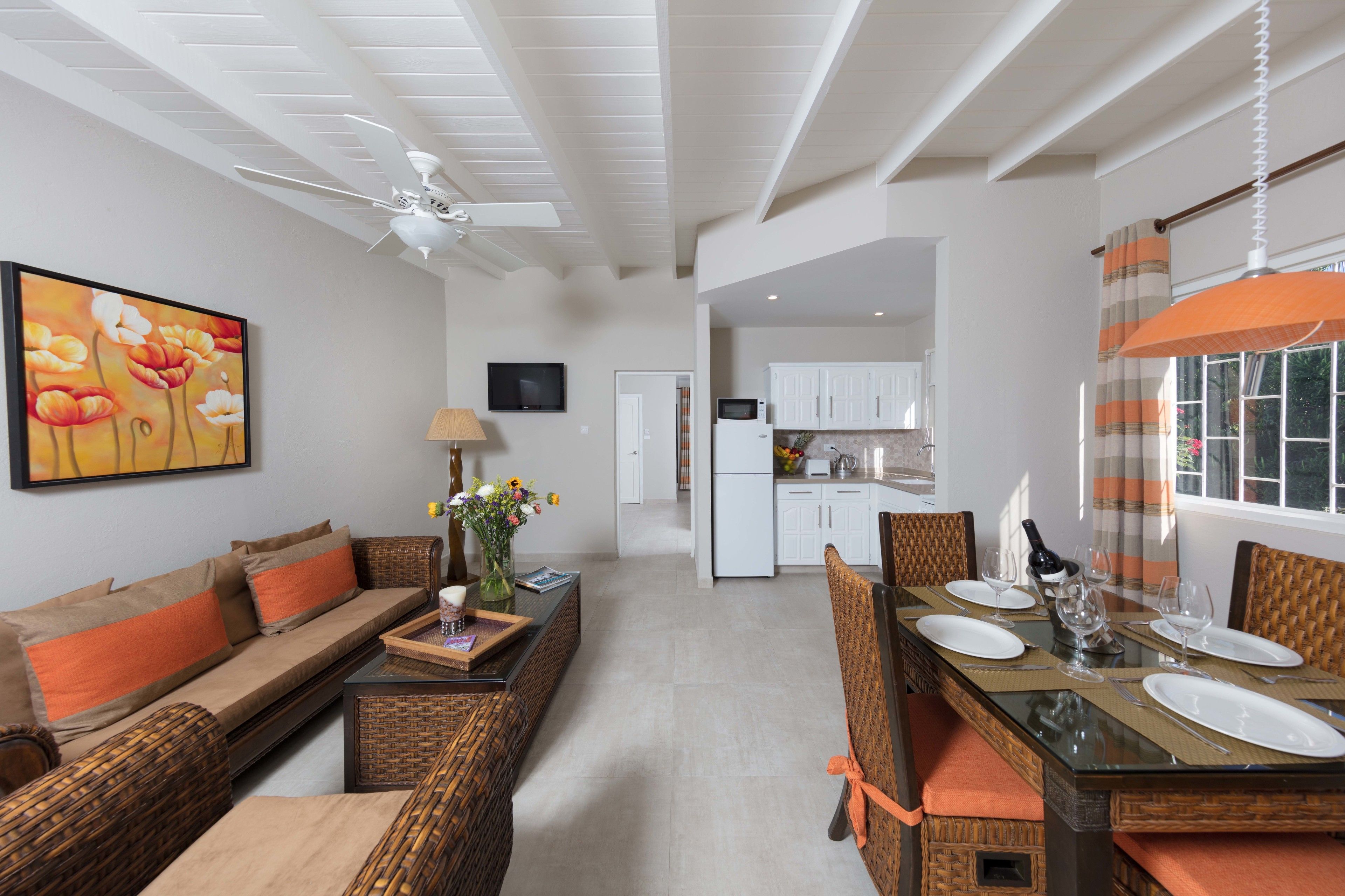 Uma sala de estar moderna com um sofá, uma mesa de jantar para quatro pessoas e uma cozinha ao fundo.