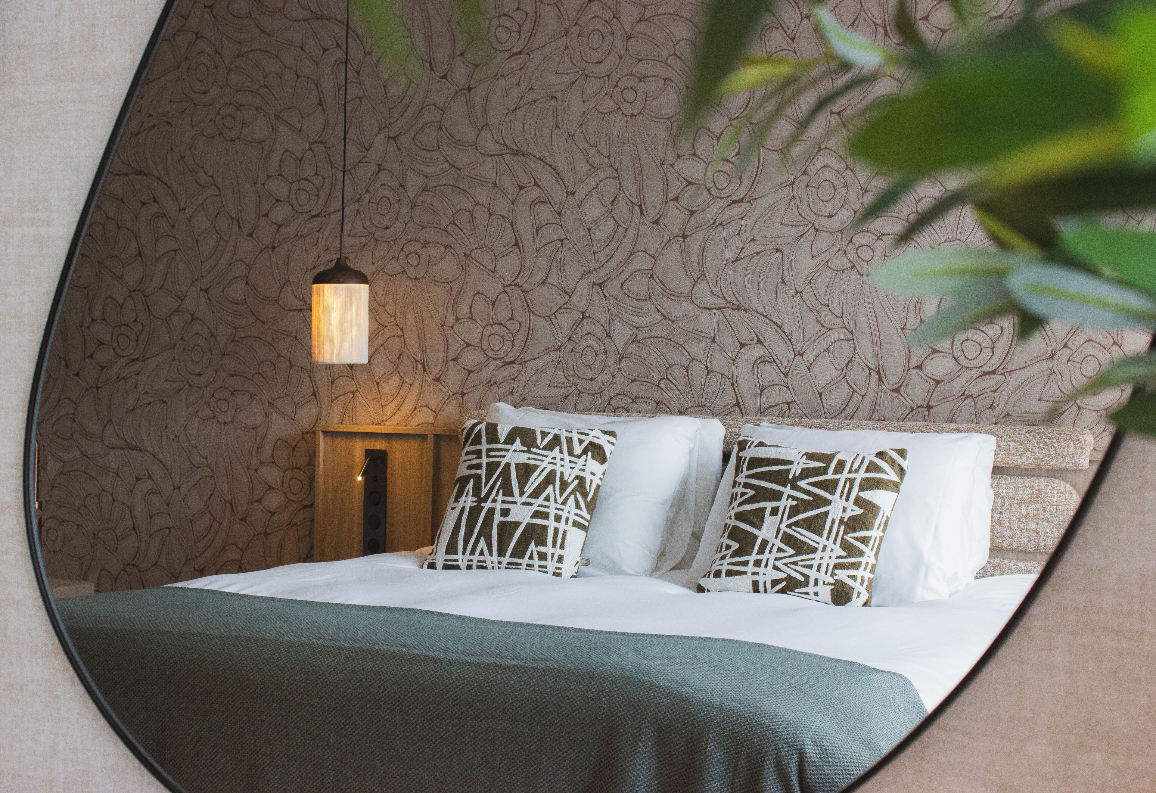 Cama bem arrumada com almofadas estampadas, abajur e papel de parede floral.
