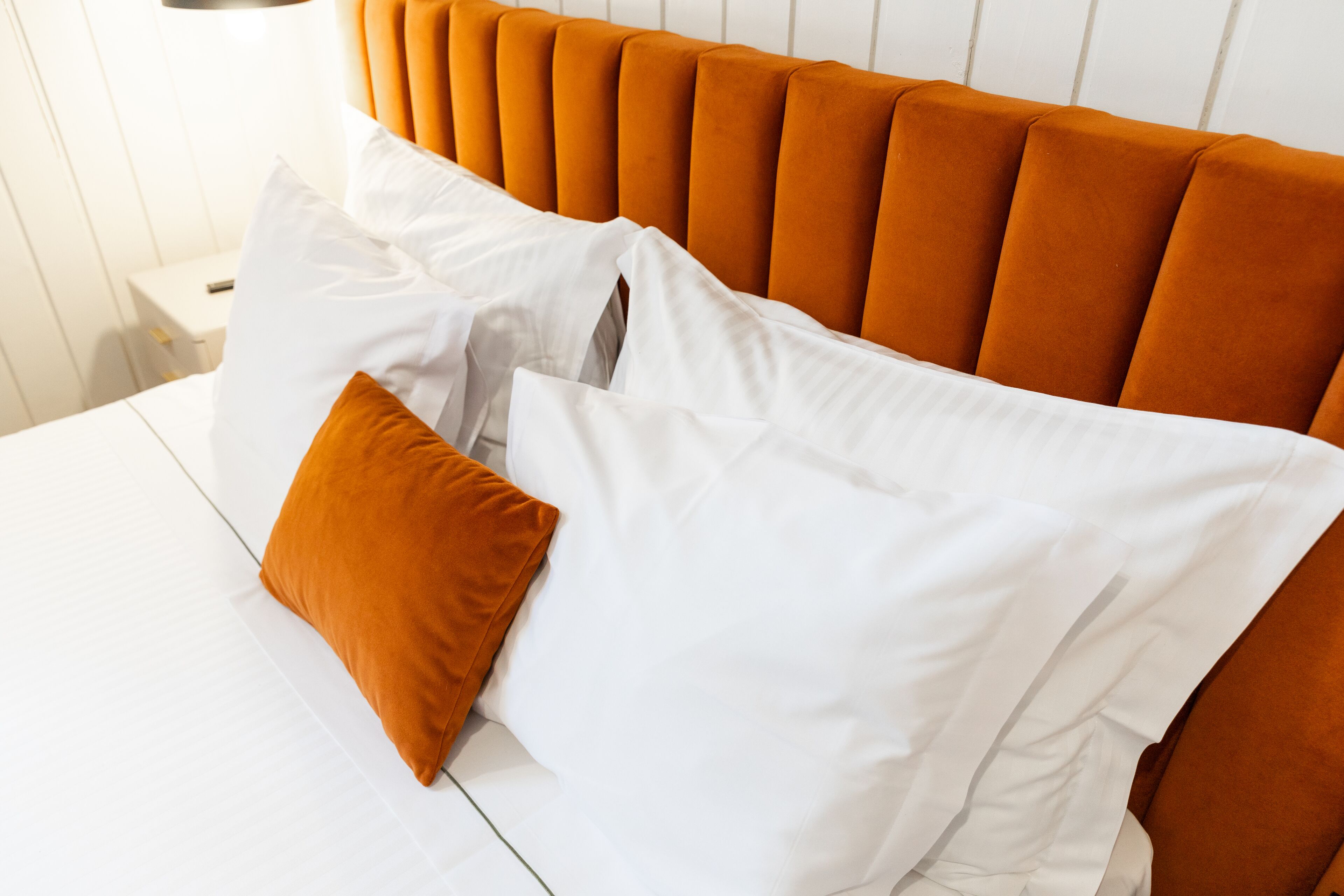 Cama com roupa de cama branca e almofadas laranja e brancas.