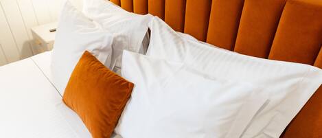 Cama com roupa de cama branca e almofadas laranja e brancas.