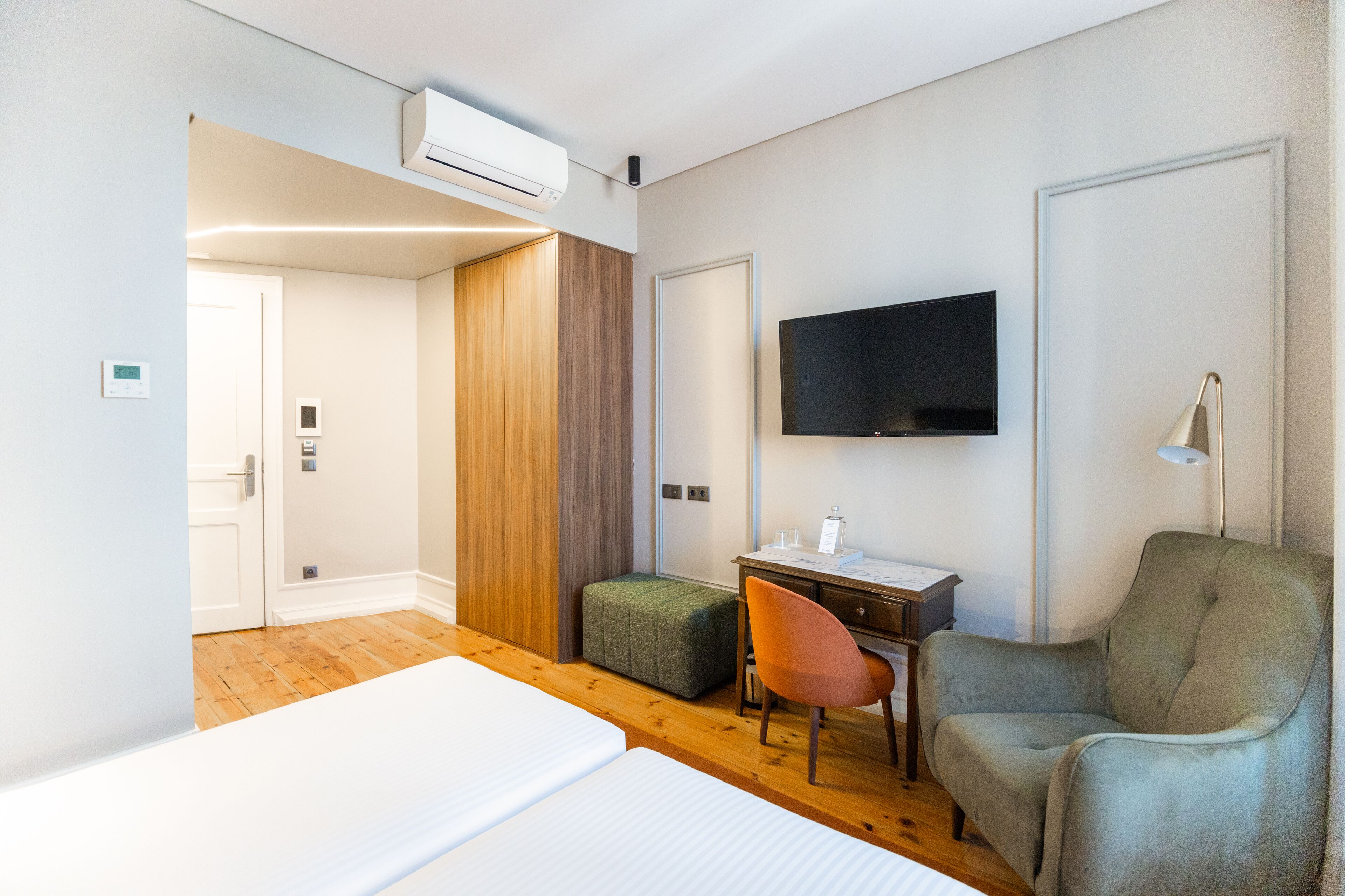 Quarto de hotel moderno com piso de madeira, uma cama, escrivaninha com cadeira, televisão e uma janela grande.