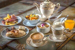 Uma mesa de café da manhã com uma chaleira, xícaras, pratos de comida e um copo de suco de laranja.