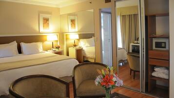 Quarto de hotel com uma cama grande, duas mesas de cabeceira com abajures, uma cadeira, um espelho e um guarda-roupa.