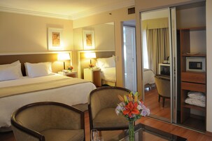 Quarto de hotel com uma cama grande, duas mesas de cabeceira com abajures, uma cadeira, um espelho e um guarda-roupa.