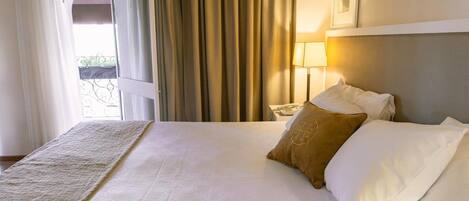 Quarto de hotel com uma cama grande, vista para o exterior através de uma janela em arco e uma luminária na mesa de cabeceira.