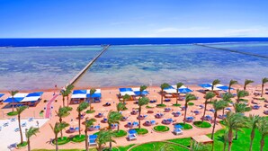 Resort à beira-mar com vários espreguiçadeiras e guarda-sóis, um cais que se estende para o mar e vista ampla do oceano.