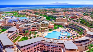 Um resort com uma grande piscina central, vários edifícios e vista para o oceano.