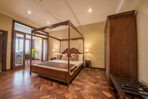 Uma cama de dossel com estrutura e cabeceira de madeira, um banco de madeira e um guarda-roupa grande de madeira.