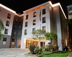 Um hotel Hampton Inn & Suites com fachada moderna, várias janelas e entrada bem iluminada.