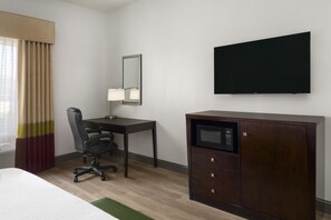 Quarto de hotel com cama, escrivaninha e cadeira, televisão de tela plana, micro-ondas e espelho.