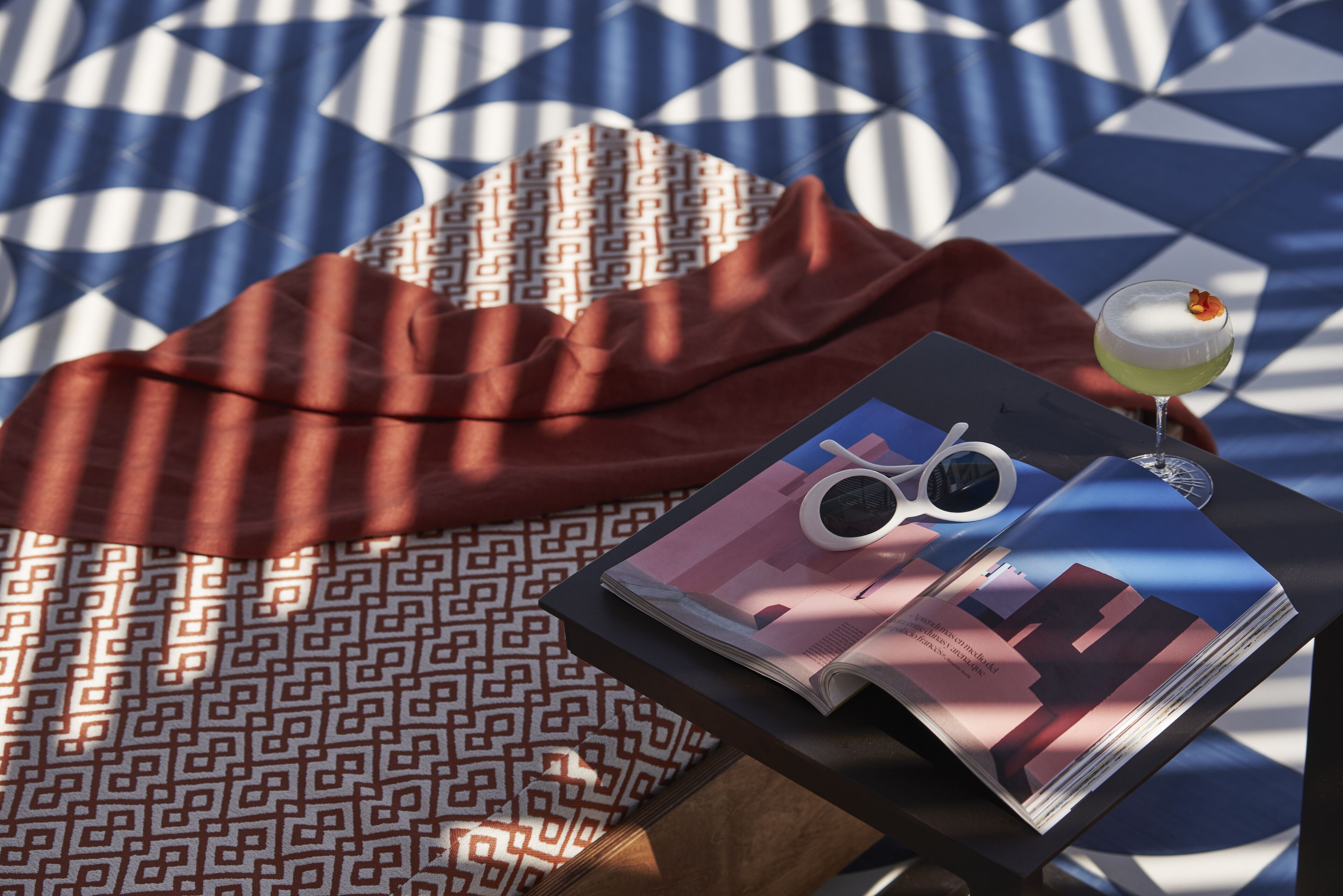 Revista com óculos de sol, uma manta e uma bebida sobre a mesa.