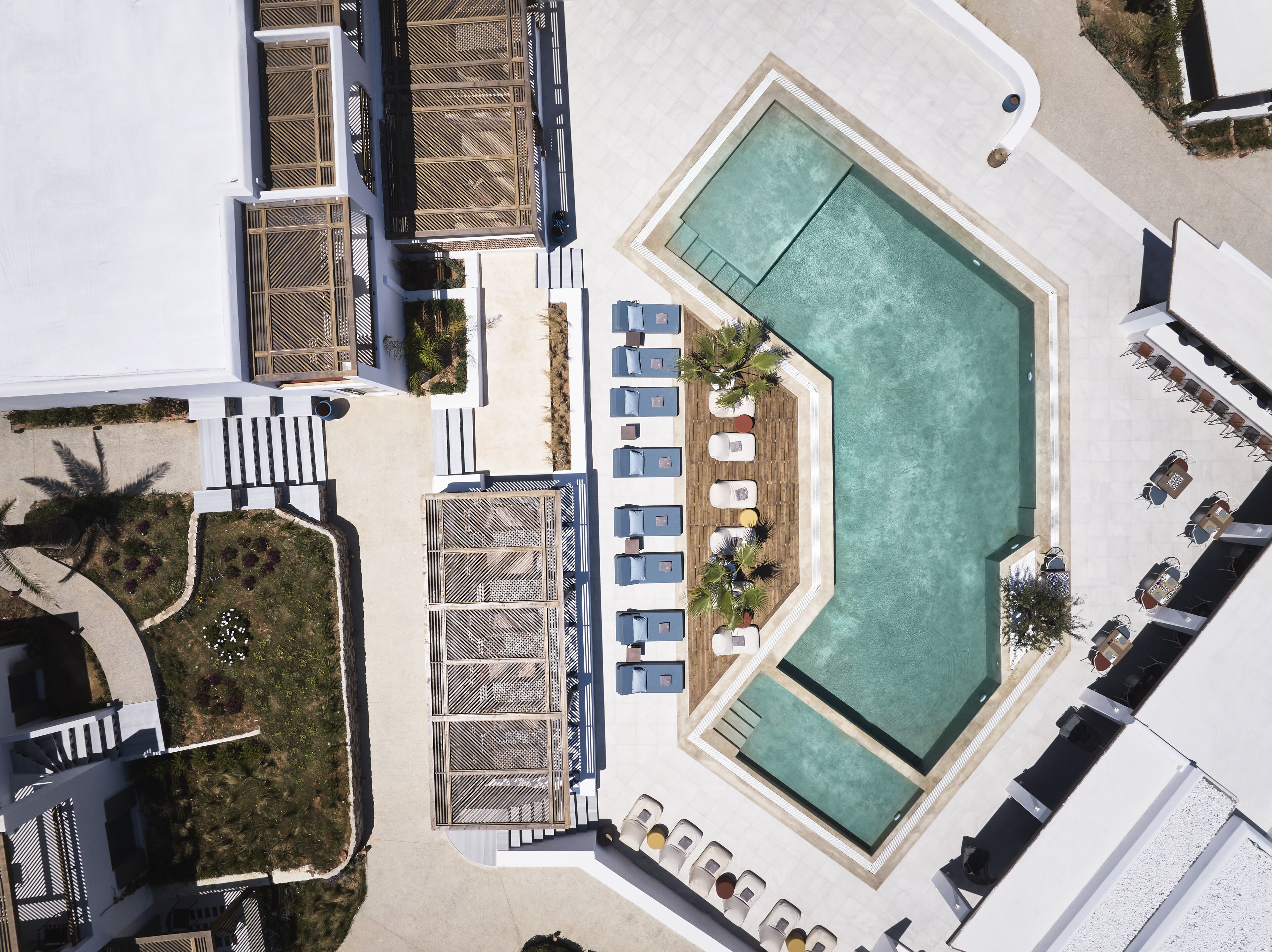 Vista aérea de um resort com uma grande piscina retangular, várias áreas de descanso com assentos e um jardim bem cuidado.