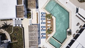 Vista aérea de um resort com uma grande piscina retangular, várias áreas de descanso com assentos e um jardim bem cuidado.
