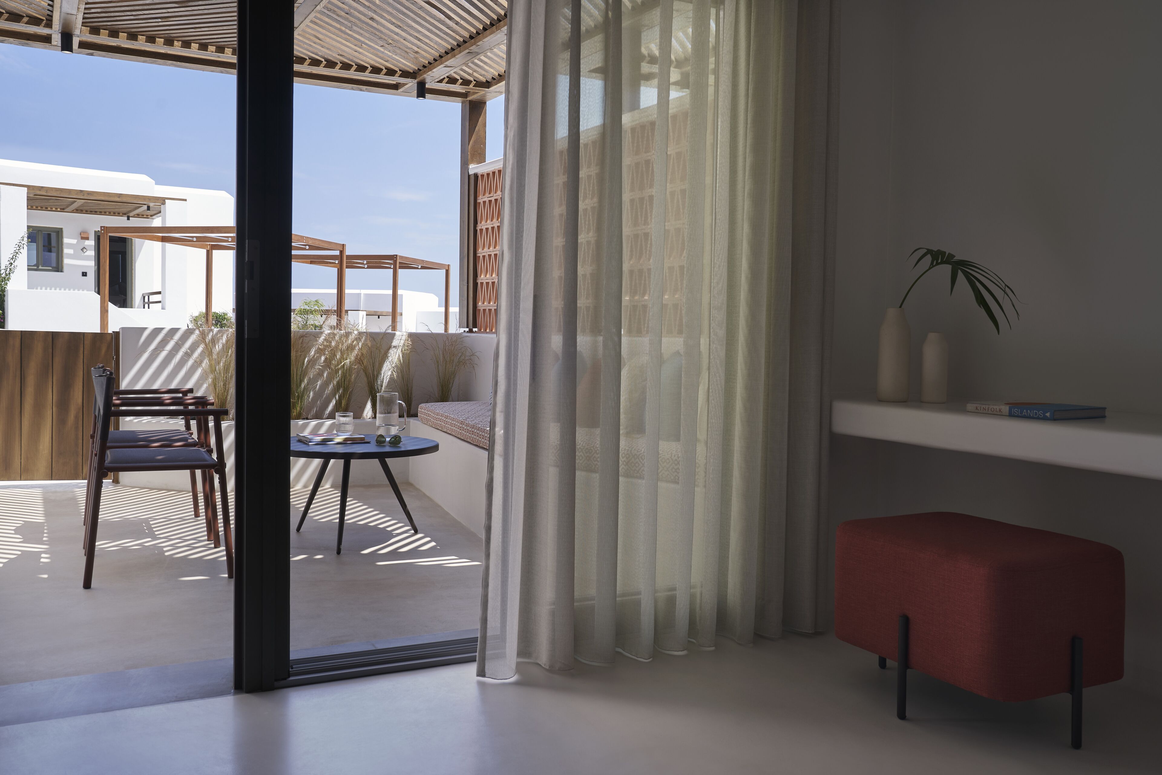 Quarto moderno com porta de correr de vidro que dá para uma área de estar ao ar livre, um banco vermelho e uma prateleira com objetos decorativos.