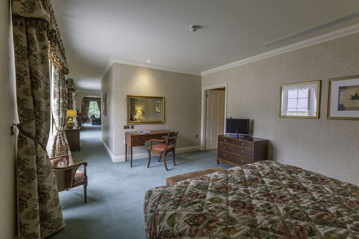 Quarto de hotel com cama, escrivaninha com cadeira, cômoda e televisão.