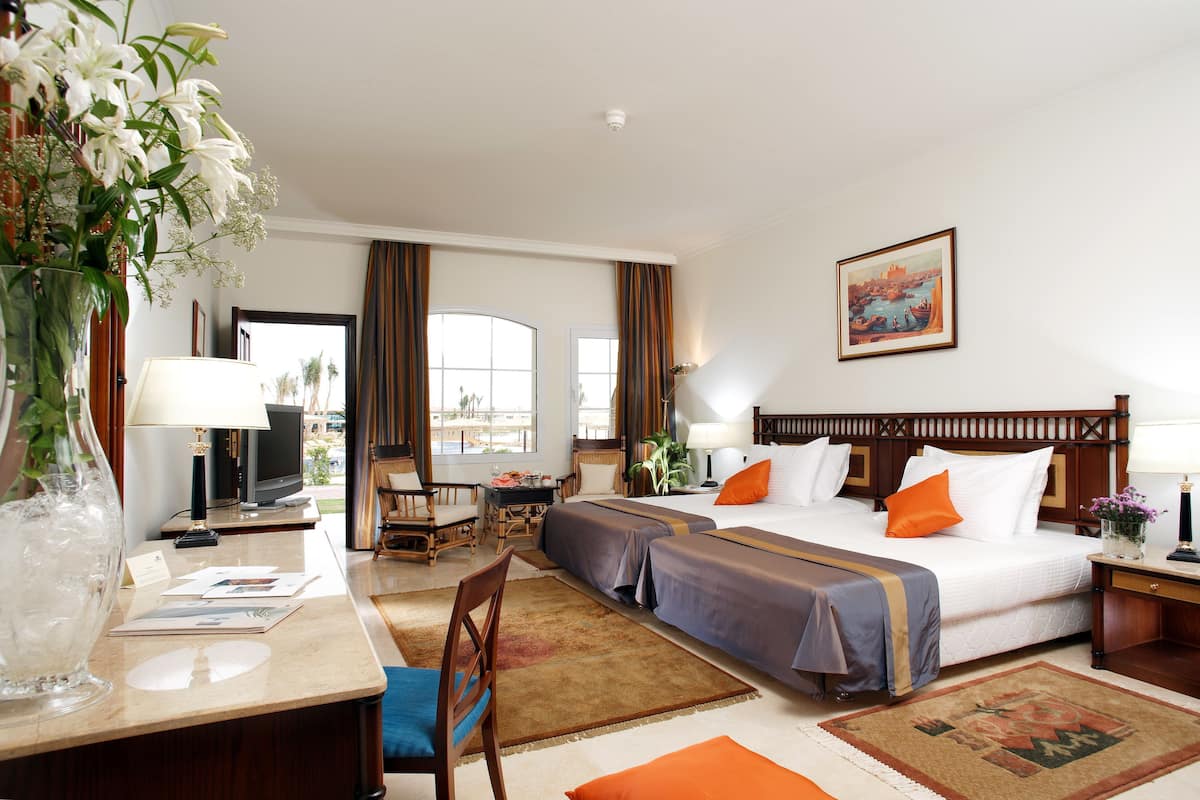 Quarto de hotel com cama, escrivaninha, cadeira, televisão e janela com cortinas.