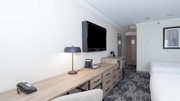Quarto de hotel com cama, escrivaninha com luminária, televisão, cafeteira e telefone.