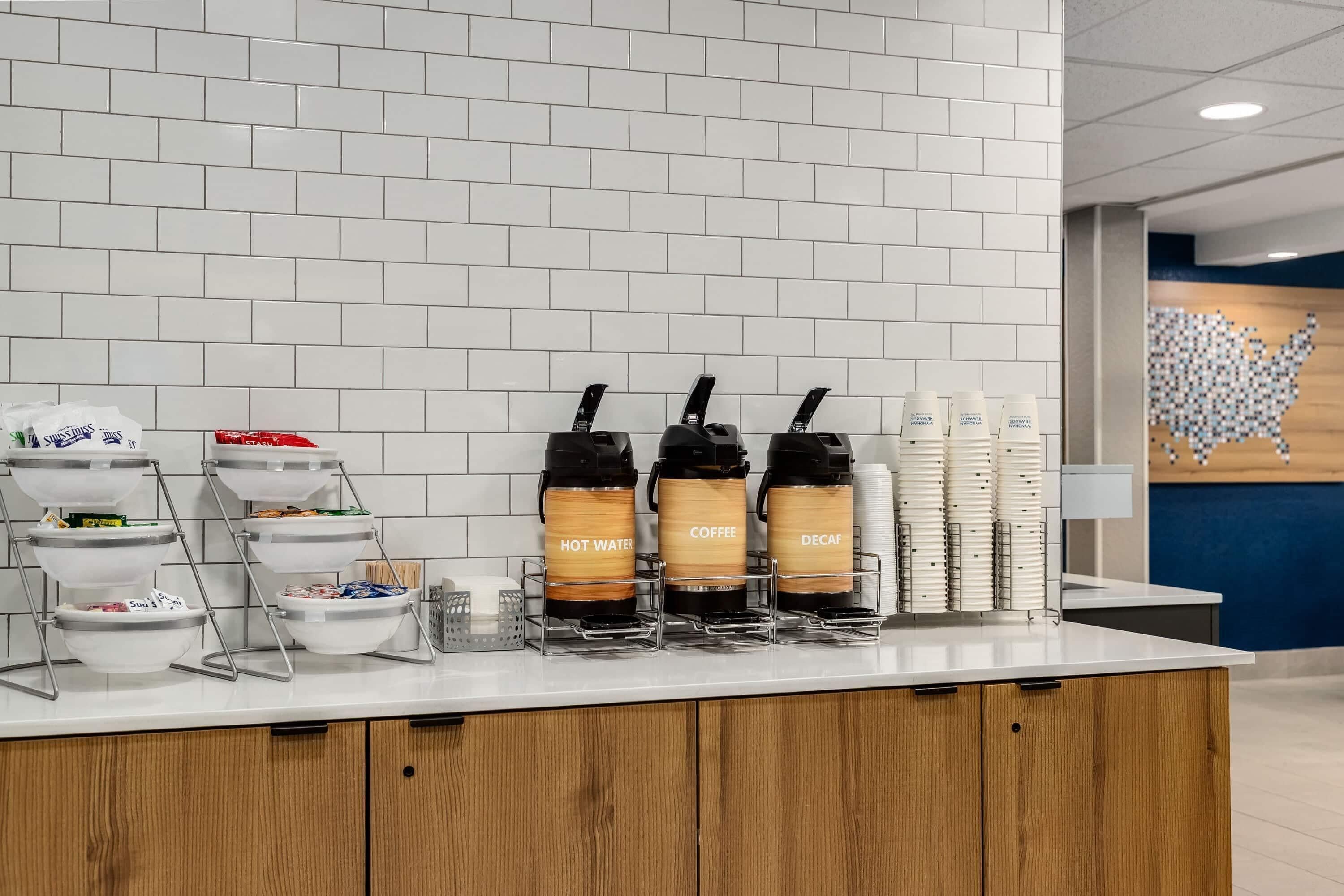 Uma estação de bebidas com serviço próprio, com dosadores identificados para água quente, café e café descafeinado.