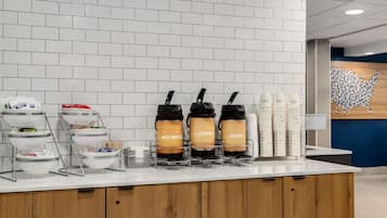 Uma estação de bebidas com serviço próprio, com dosadores identificados para água quente, café e café descafeinado.