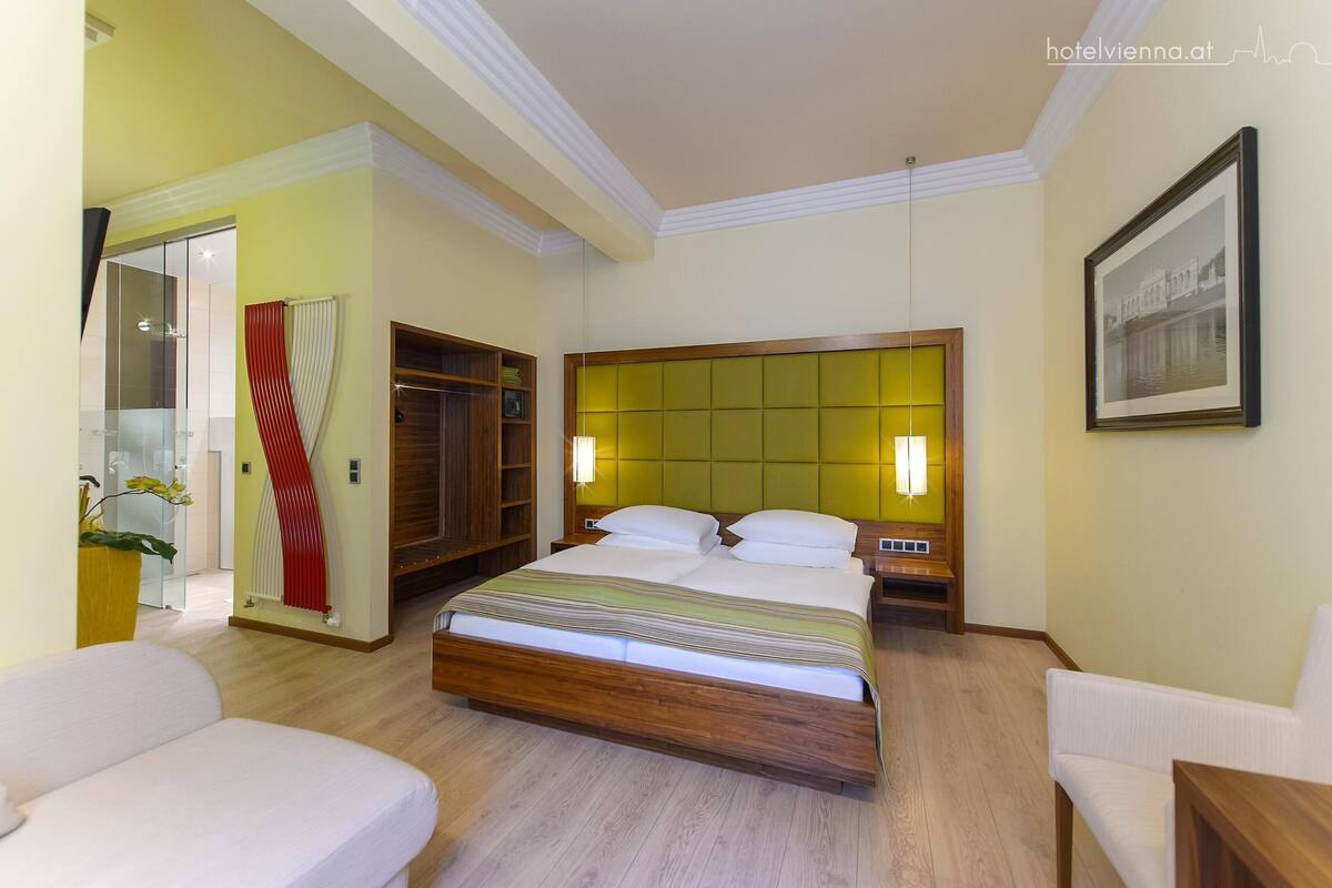 Quarto de hotel com uma cama grande, mesa de cabeceira, uma cadeira, guarda-roupa e espelho.