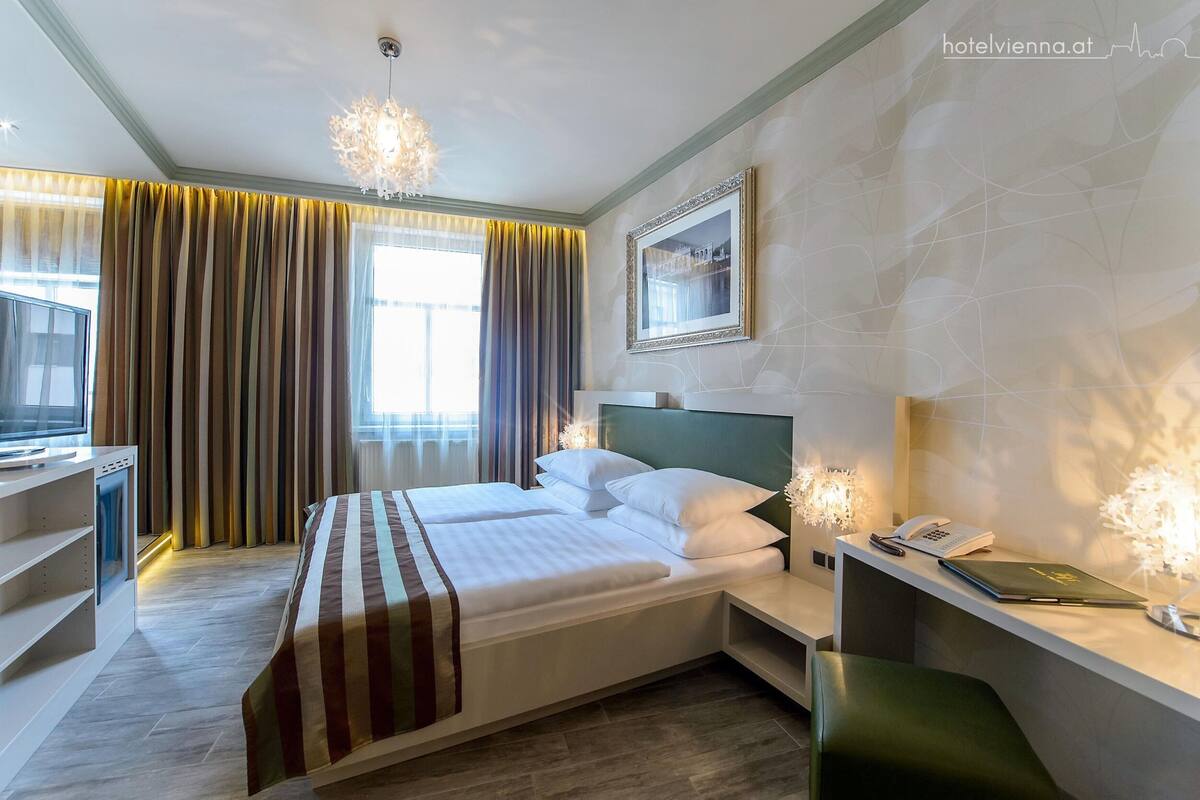 Quarto de hotel com cama, mesas de cabeceira, escrivaninha e uma cadeira.