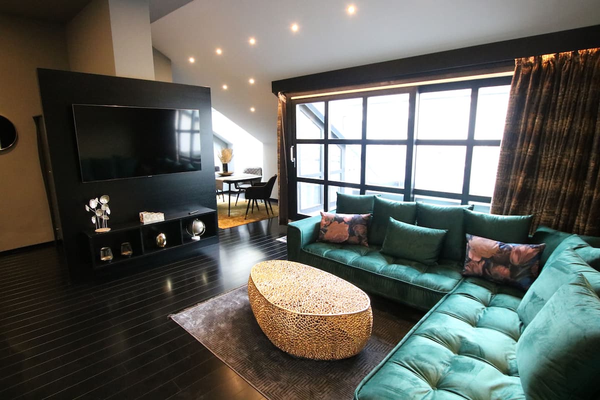 Uma sala de estar moderna com uma televisão de tela grande, um sofá verde e um banquinho trançado.