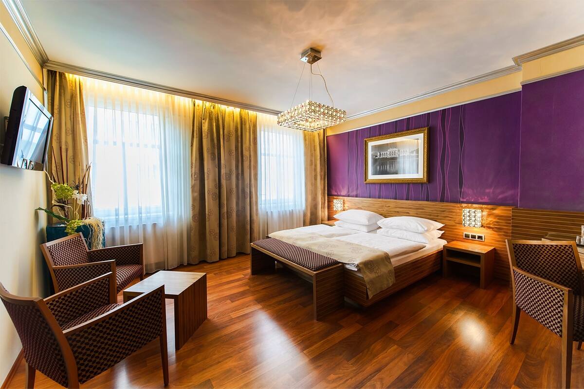 Quarto de hotel com cama, piso de madeira, televisão, um banco e uma cadeira.