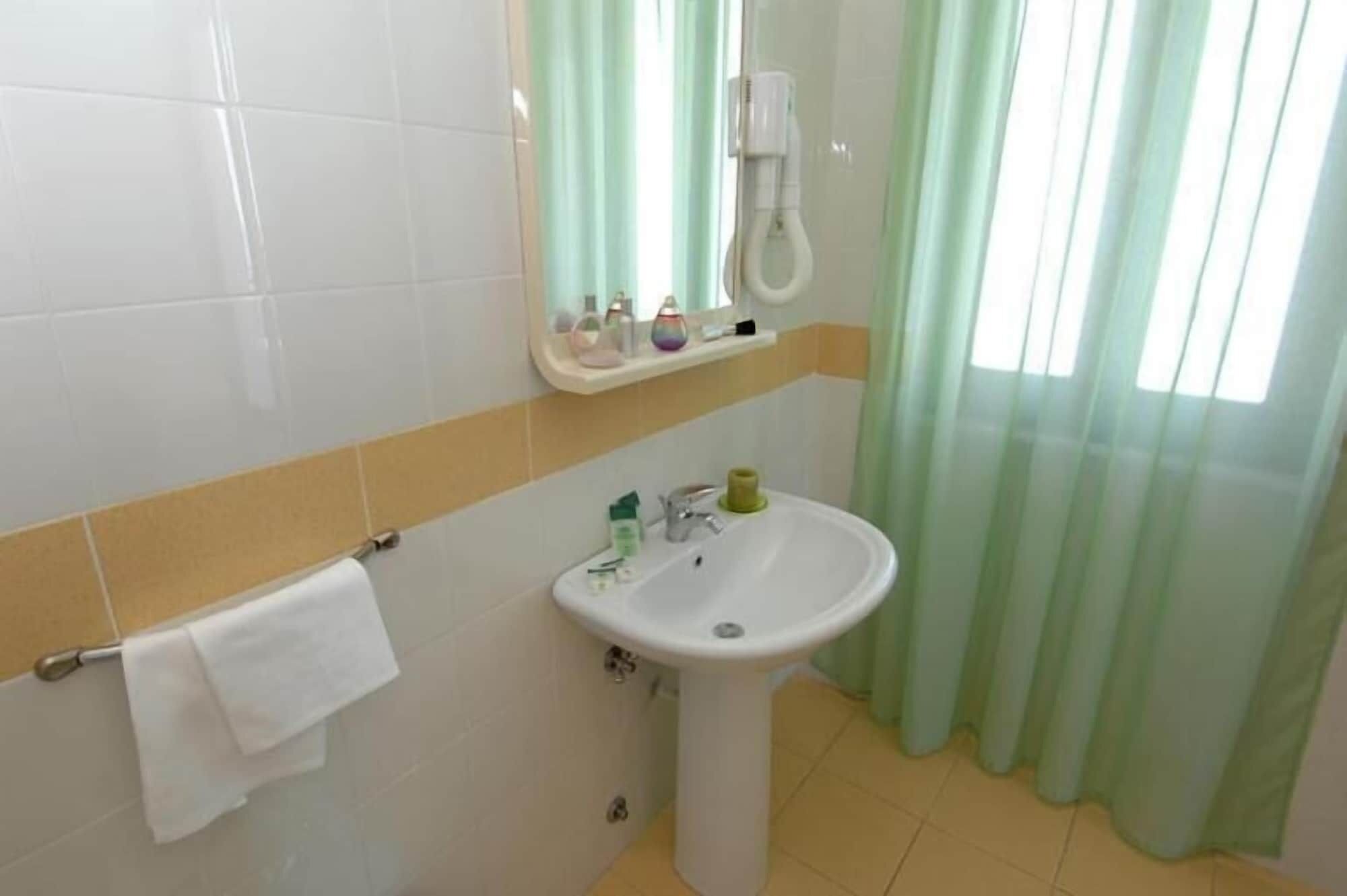 Casa de banho com uma pia branca, um espelho e um porta-toalhas.