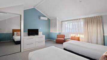Quarto de hotel com uma cama, televisão sobre um aparador, uma cadeira e uma janela com cortinas.
