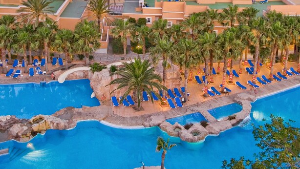 Resort com área de piscina, palmeiras e vista para o oceano.