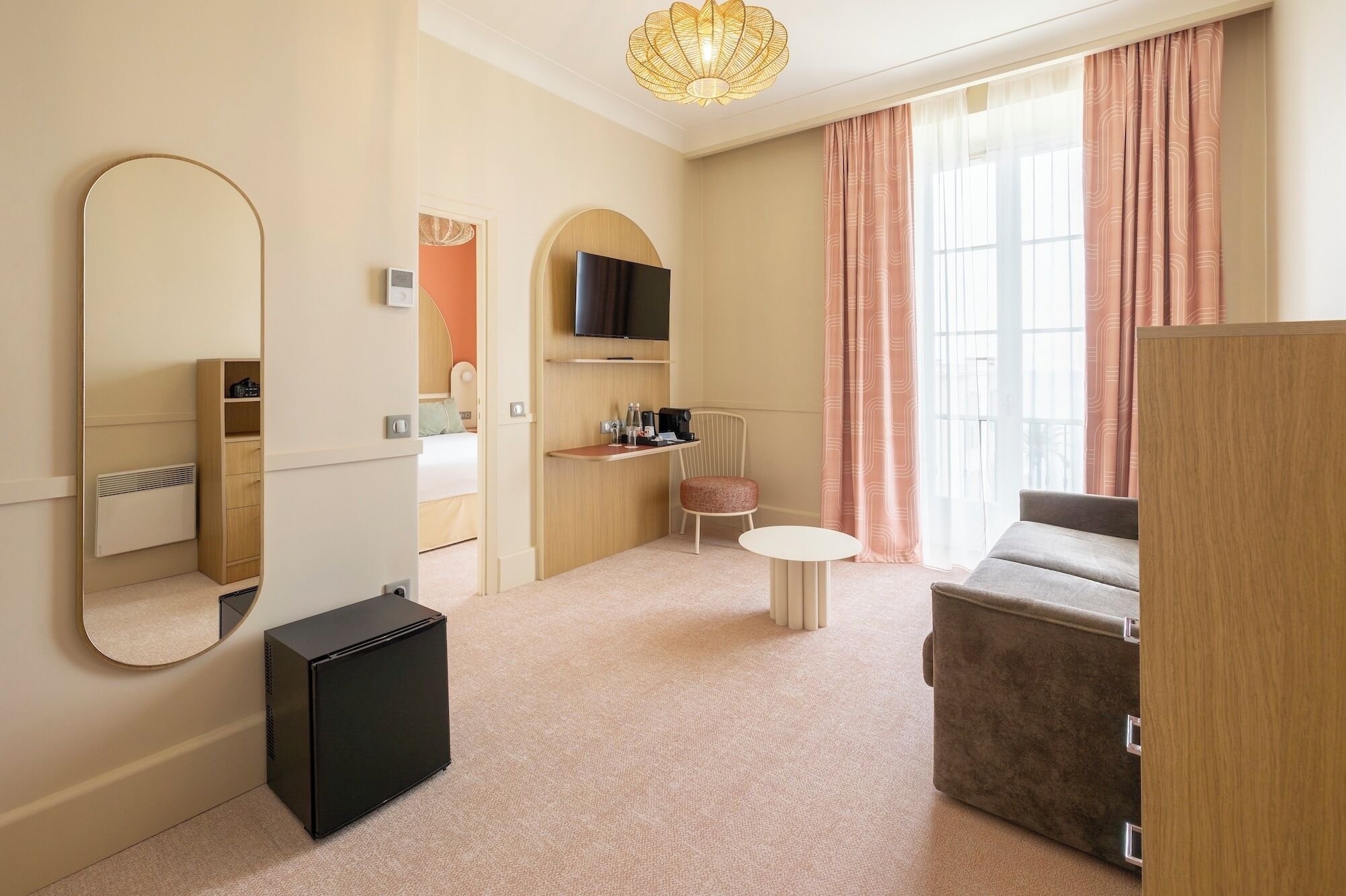 Quarto de hotel com cama, televisão, mesinha, cadeira, guarda-roupa e espelho.