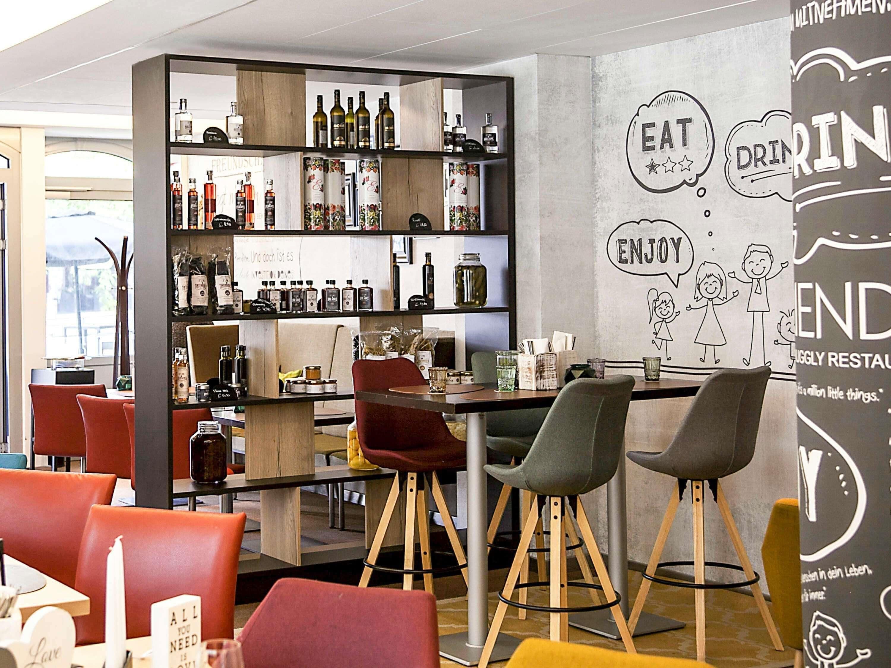 Interior de restaurante com área de bar, mesas e cadeiras, e uma parede com frases motivacionais.