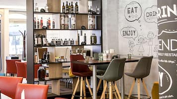 Interior de restaurante com área de bar, mesas e cadeiras, e uma parede com frases motivacionais.