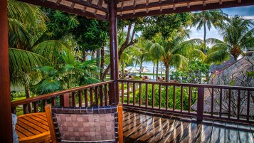 Um deck de madeira com um banco revestido de azulejos, cercado por vegetação tropical exuberante e com vista para uma área de piscina.