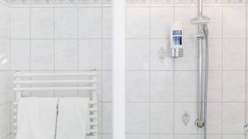 Casa de banho com azulejos brancos, chuveiro com duche manual e toalheiro com duas toalhas brancas.