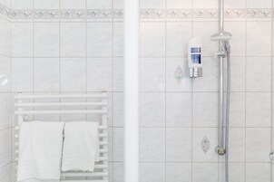 Casa de banho com azulejos brancos, chuveiro com duche manual e toalheiro com duas toalhas brancas.