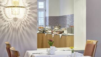 Espaço de refeições com lustre, balcão de buffet e mesa posta para dois.